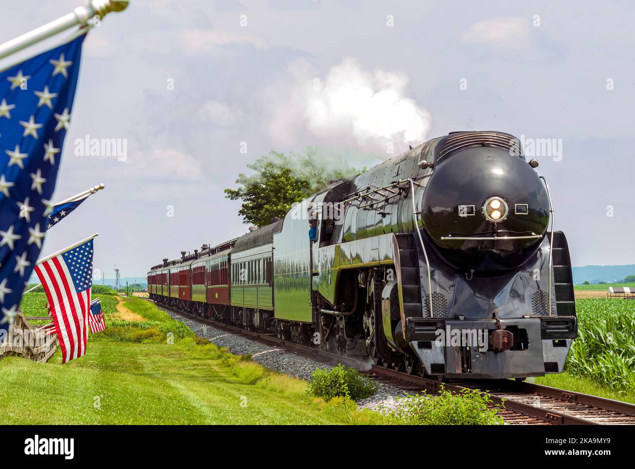 A Restored Steam Passenger Train Approaches As American Flags Wave on a ...