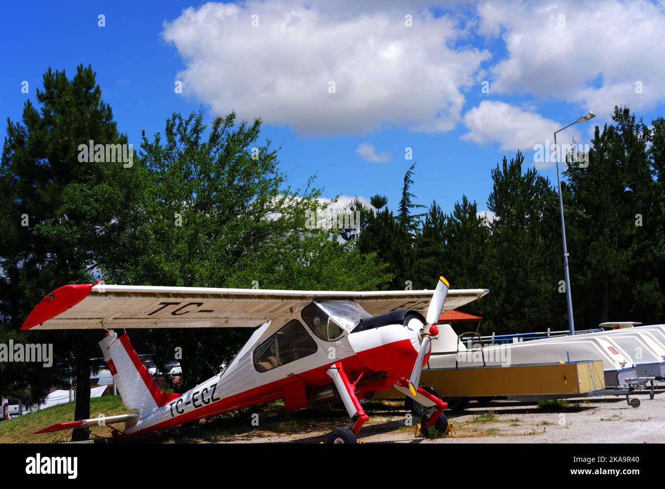 White plane parked within trees in a sunny day outdoor with cloudy sky ...