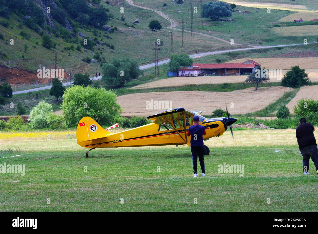 Yellow plane parked on grass with people around it on grass in a sunny ...