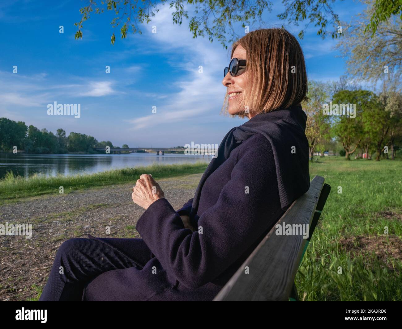 adult mature elegant caucasian woman sitting on a park bench with legs ...
