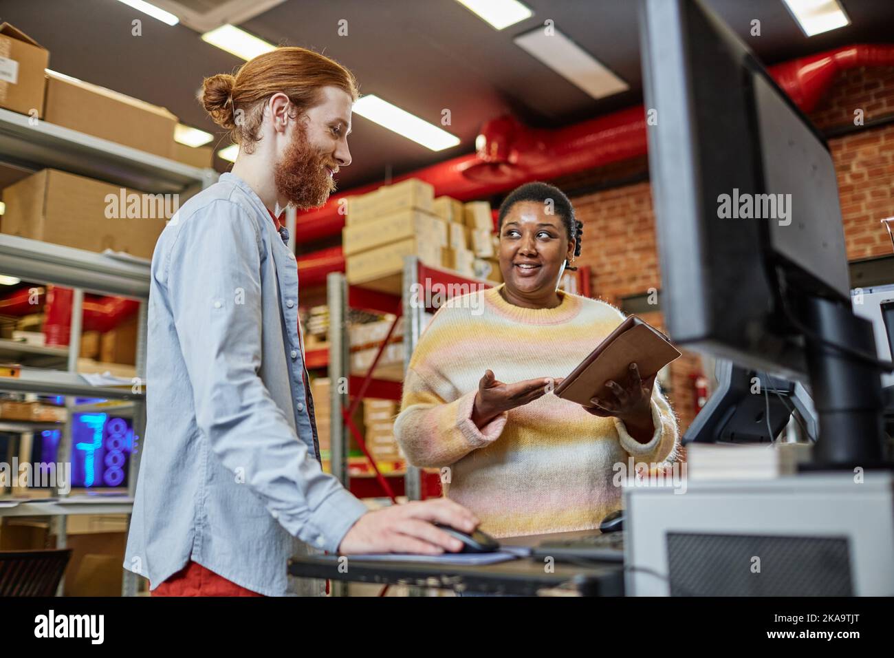 Portrait of two young people working in print shop and using computer ...
