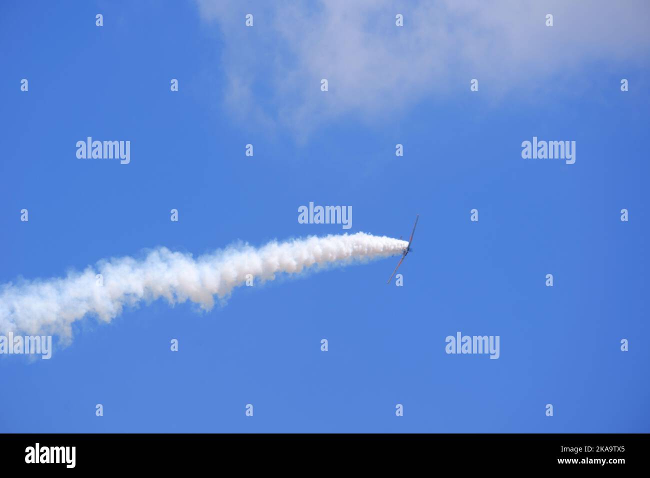 Plane flying with smoke on tail at blue sky with clouds Stock Photo - Alamy