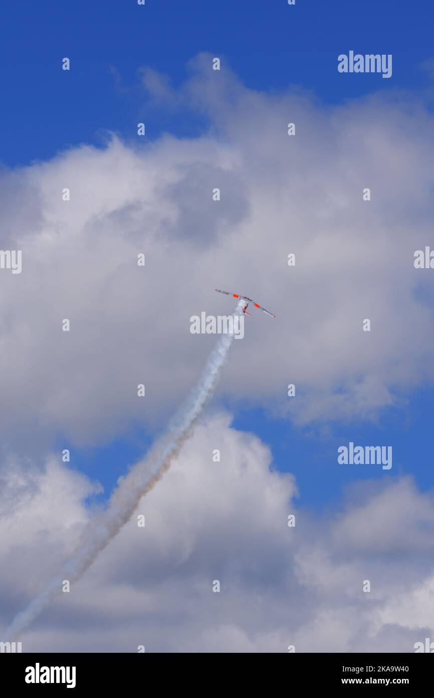Plane flying with smoke on tail at blue sky with clouds Stock Photo - Alamy