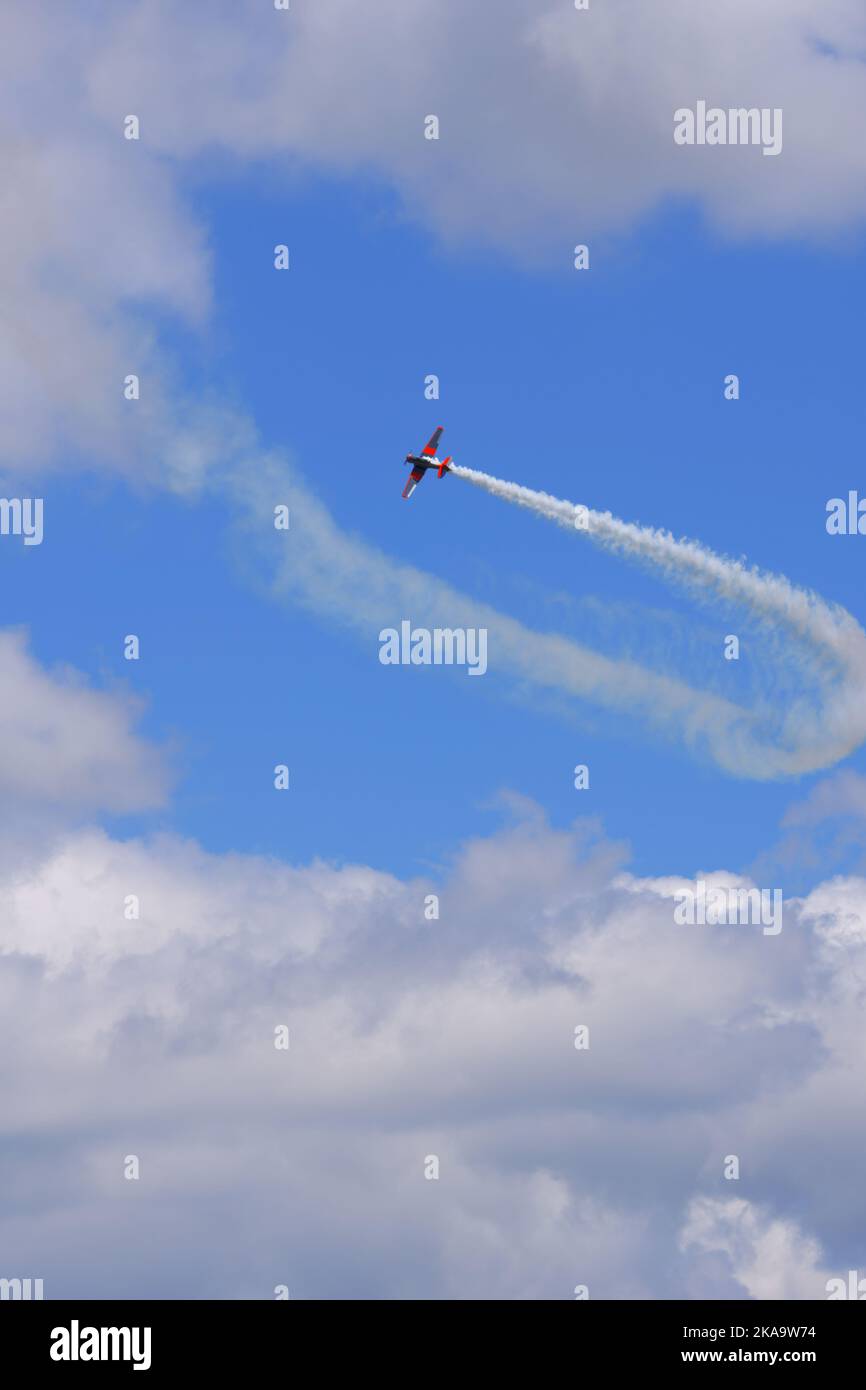 Plane flying with smoke on tail at blue sky with clouds Stock Photo - Alamy