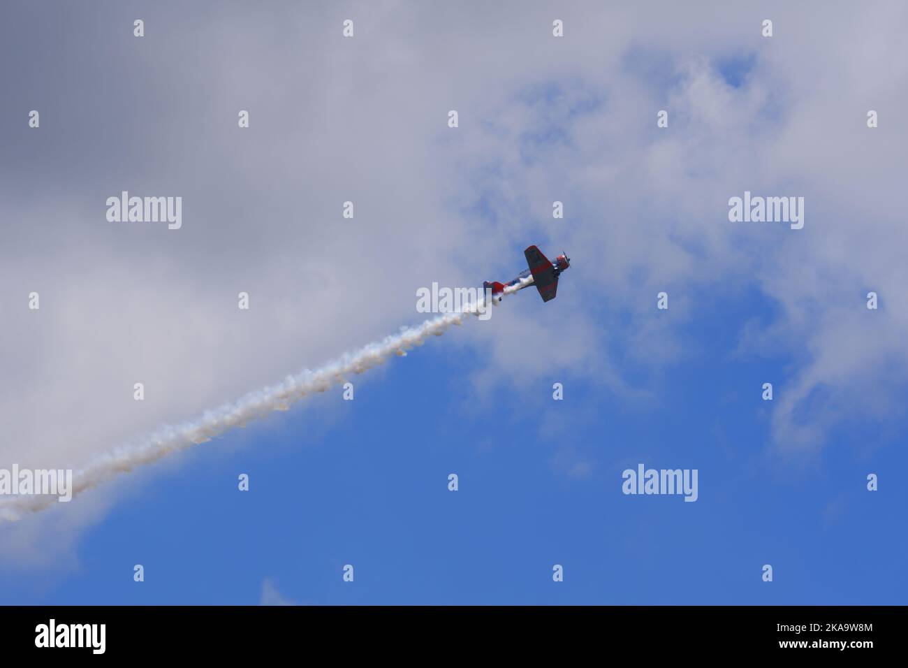 Plane flying with smoke on tail at blue sky with clouds Stock Photo - Alamy