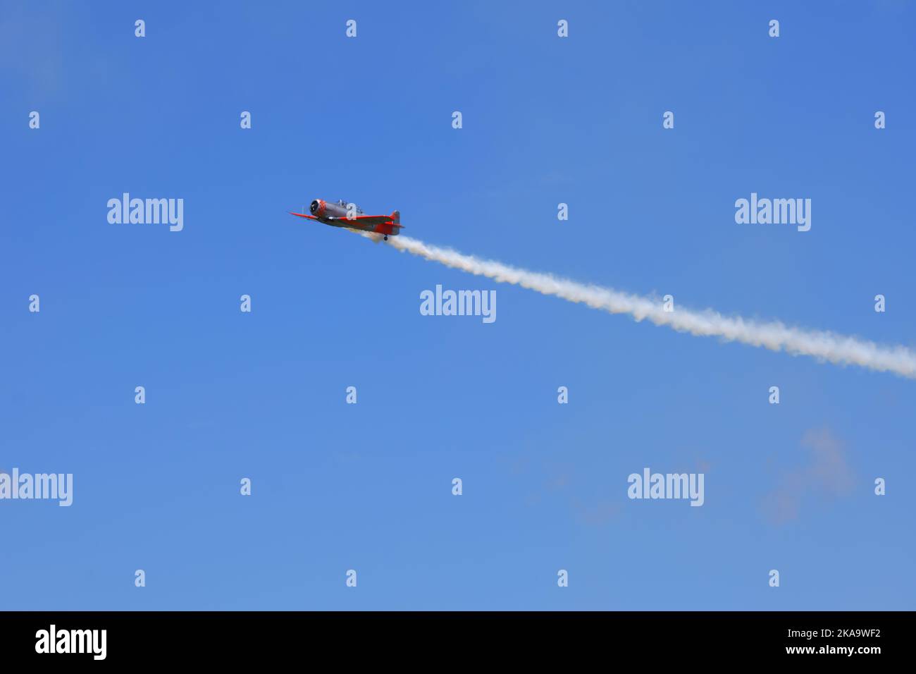 Plane flying with smoke on tail at blue sky with clouds Stock Photo - Alamy
