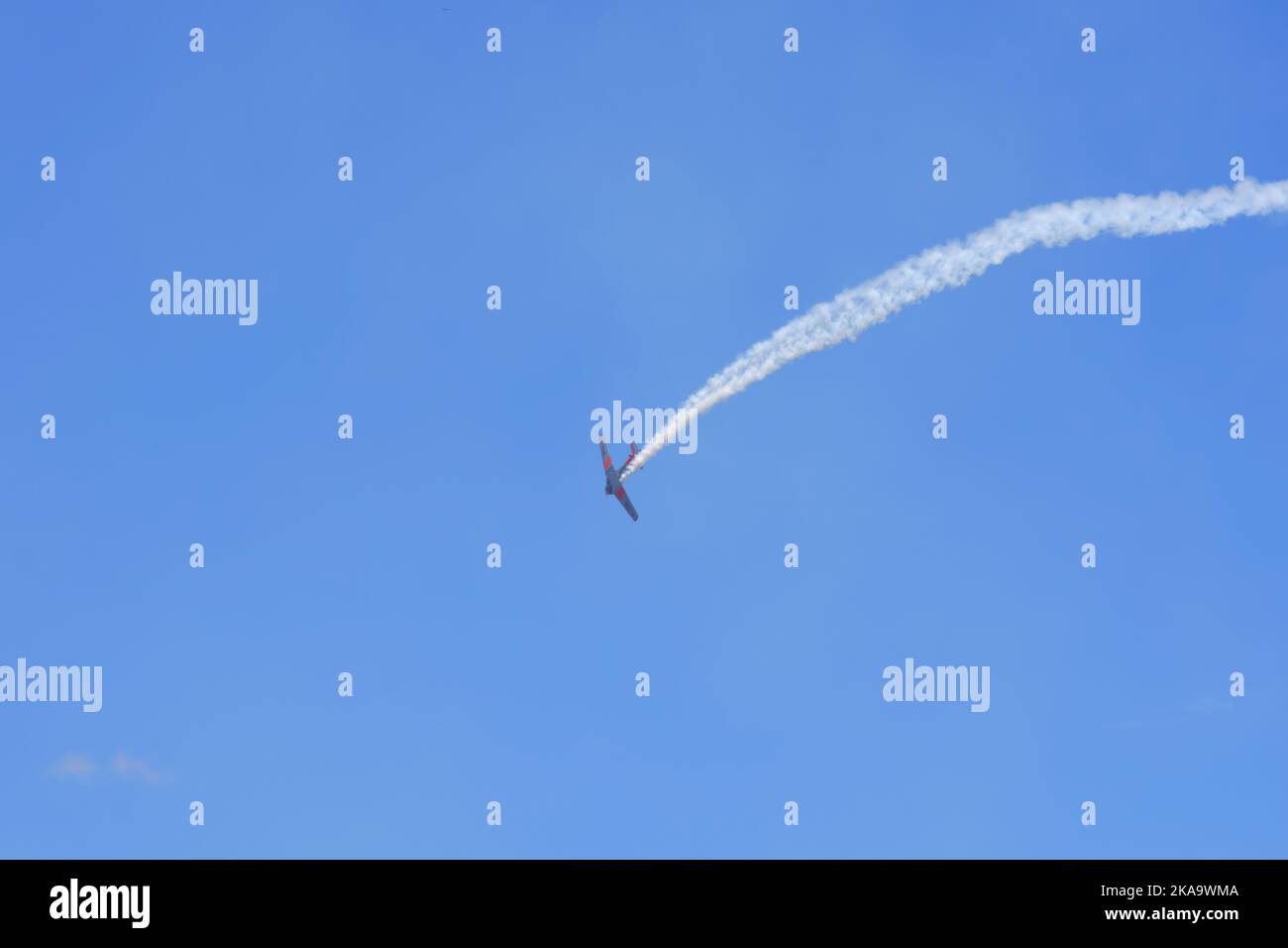 Plane flying with smoke on tail at blue sky with clouds Stock Photo - Alamy
