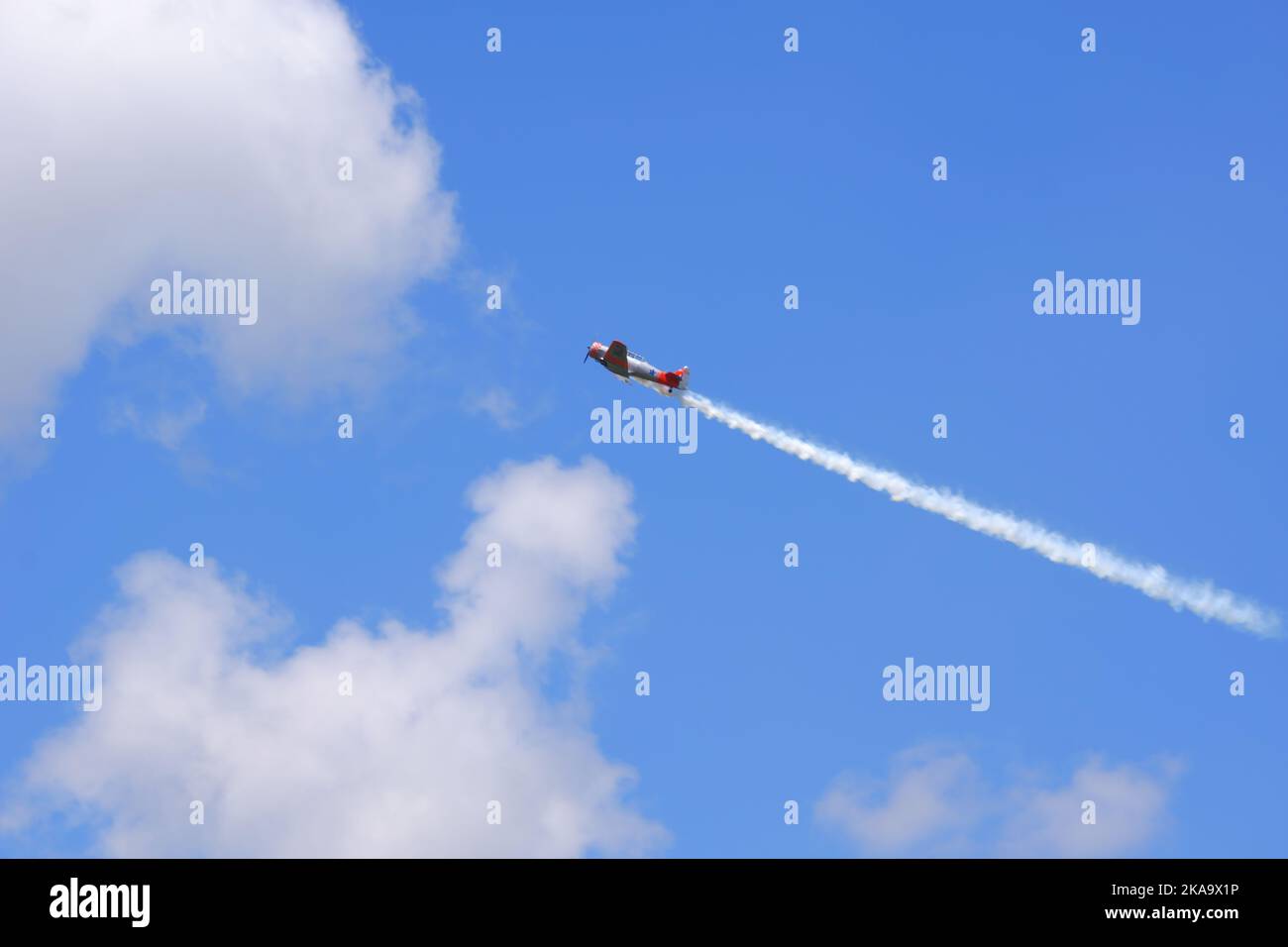 Plane flying with smoke on tail at blue sky with clouds Stock Photo - Alamy