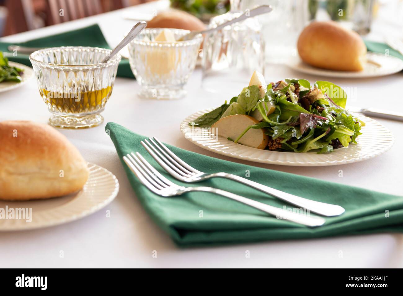 Fine dining table setting; plated salad, dinner rolls and various ...