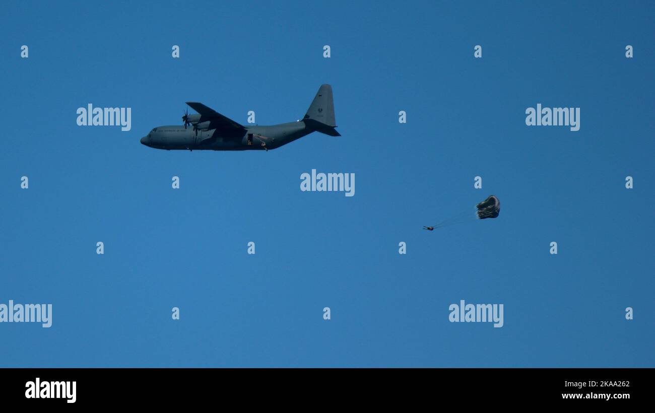 A military personnel parachuting from a RAAF aircraft in blue sky ...