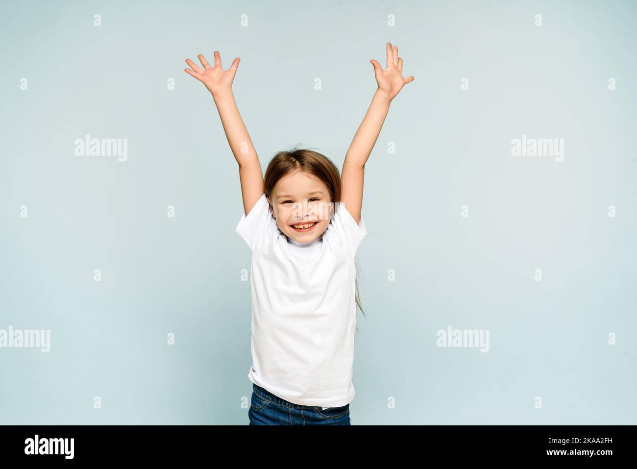 Happy little girl raising her hands up on a blue background with copy ...
