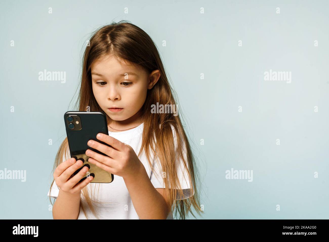 OMG, shocked little schoolgirl holding smartphone on blue background in ...
