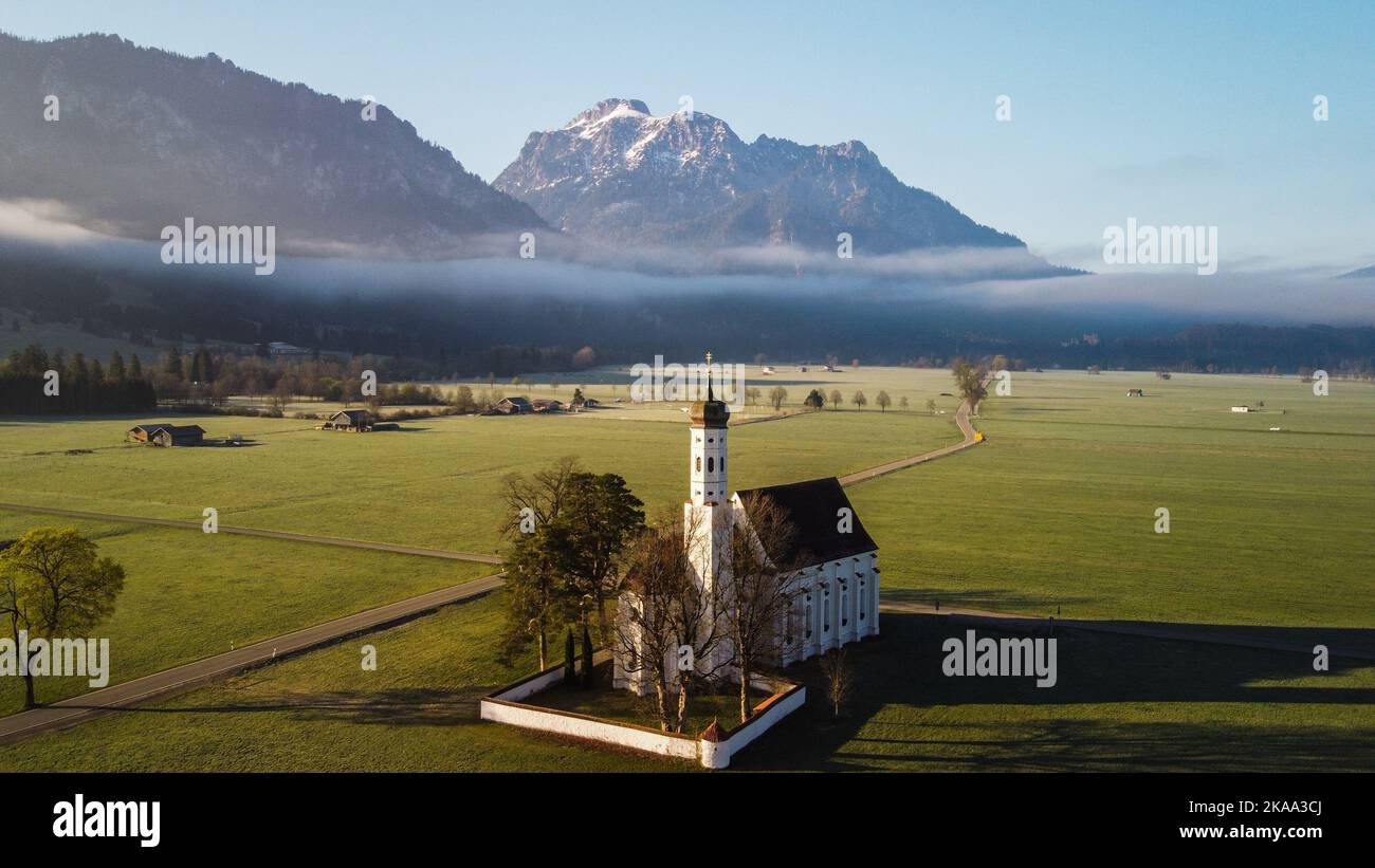 An aerial view of a white building in a field with mountains in the ...