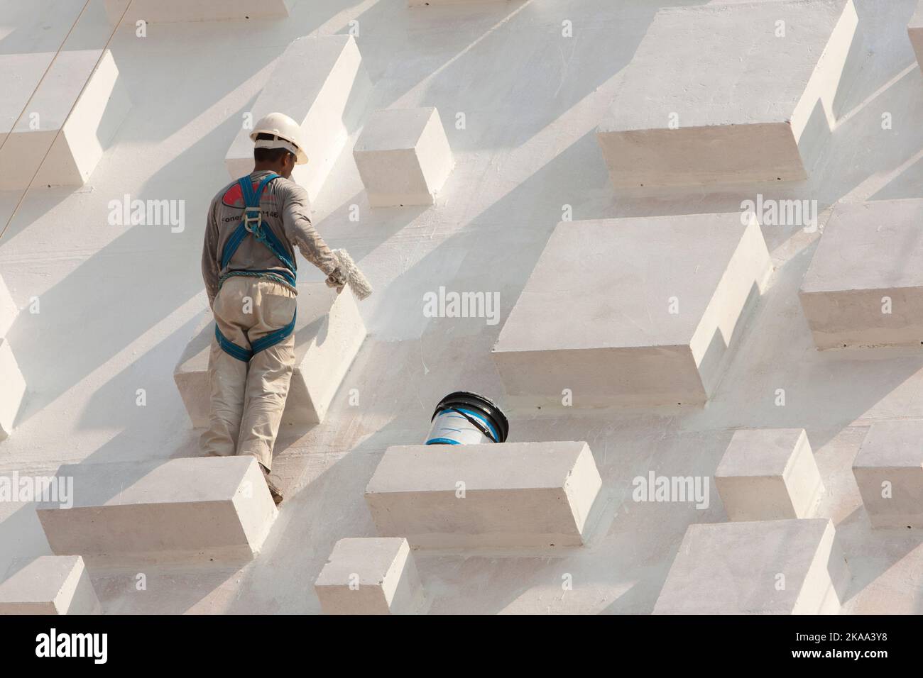 A closeup of a worker painting a modern building white in bright sunny ...