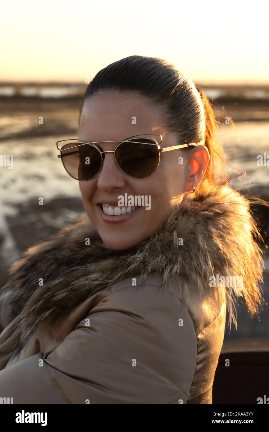 Portrait of a young caucasian woman in a golden coat and sunglasses ...