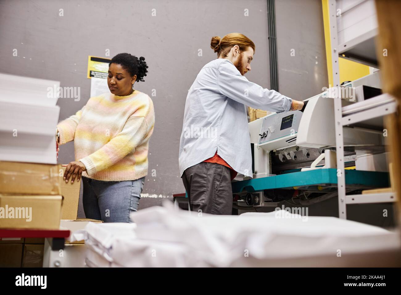 Side view of two workers operating industrial printing machine in shop ...