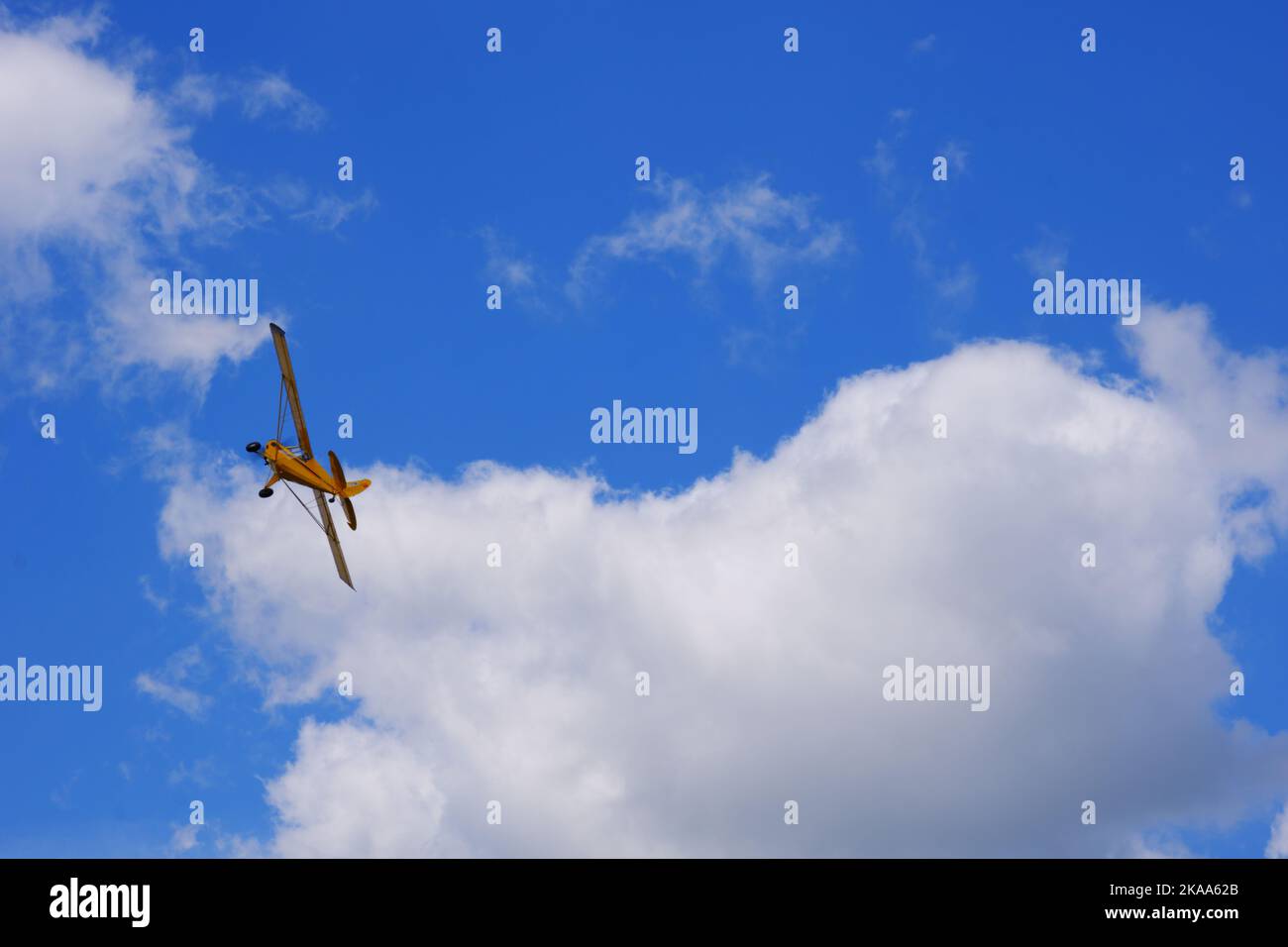 Small yellow plane at sky, having turns at blue sky with light clouds ...
