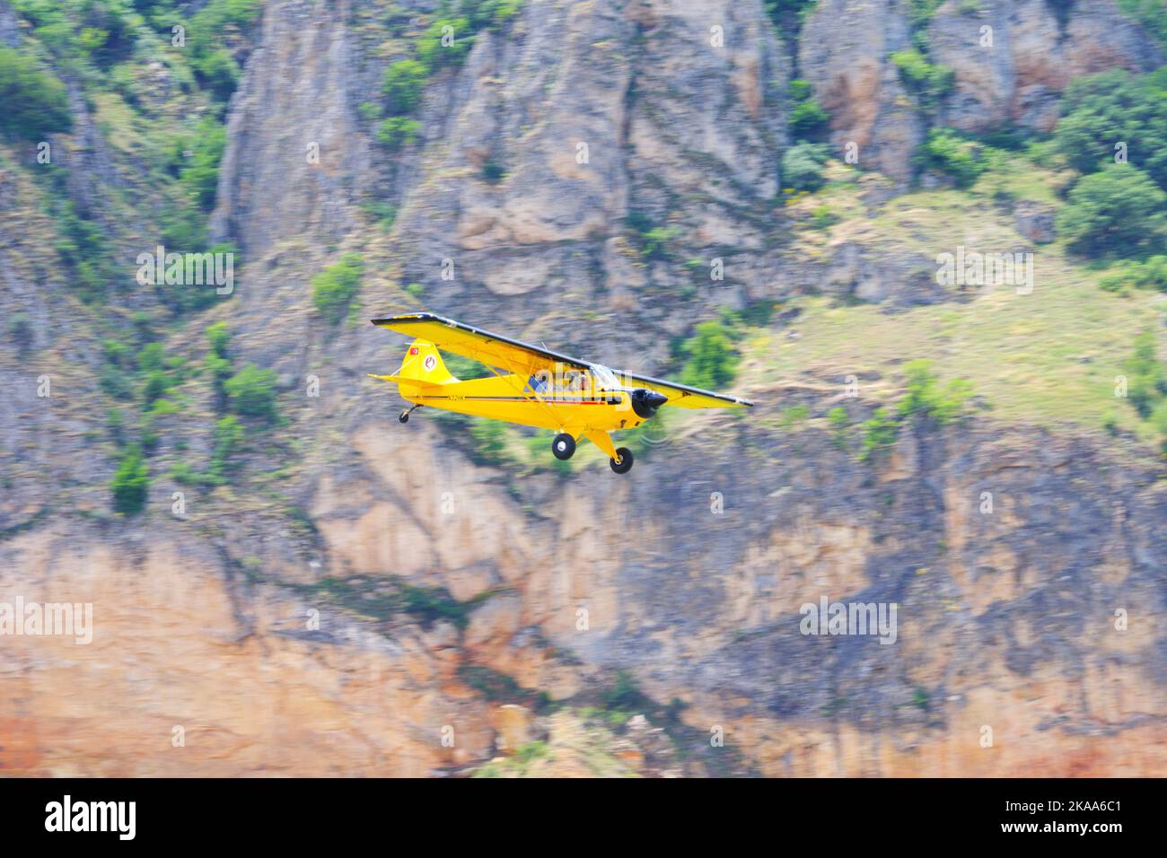 Yellow single engine plane approaching to the ground with rocks at the ...