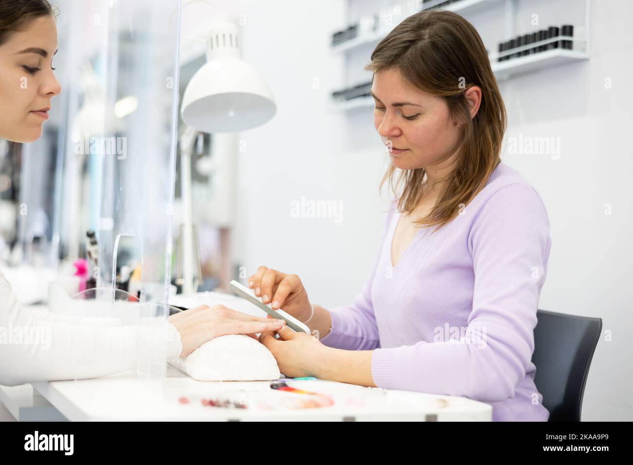Manicurist files the nails of a young female client Stock Photo - Alamy