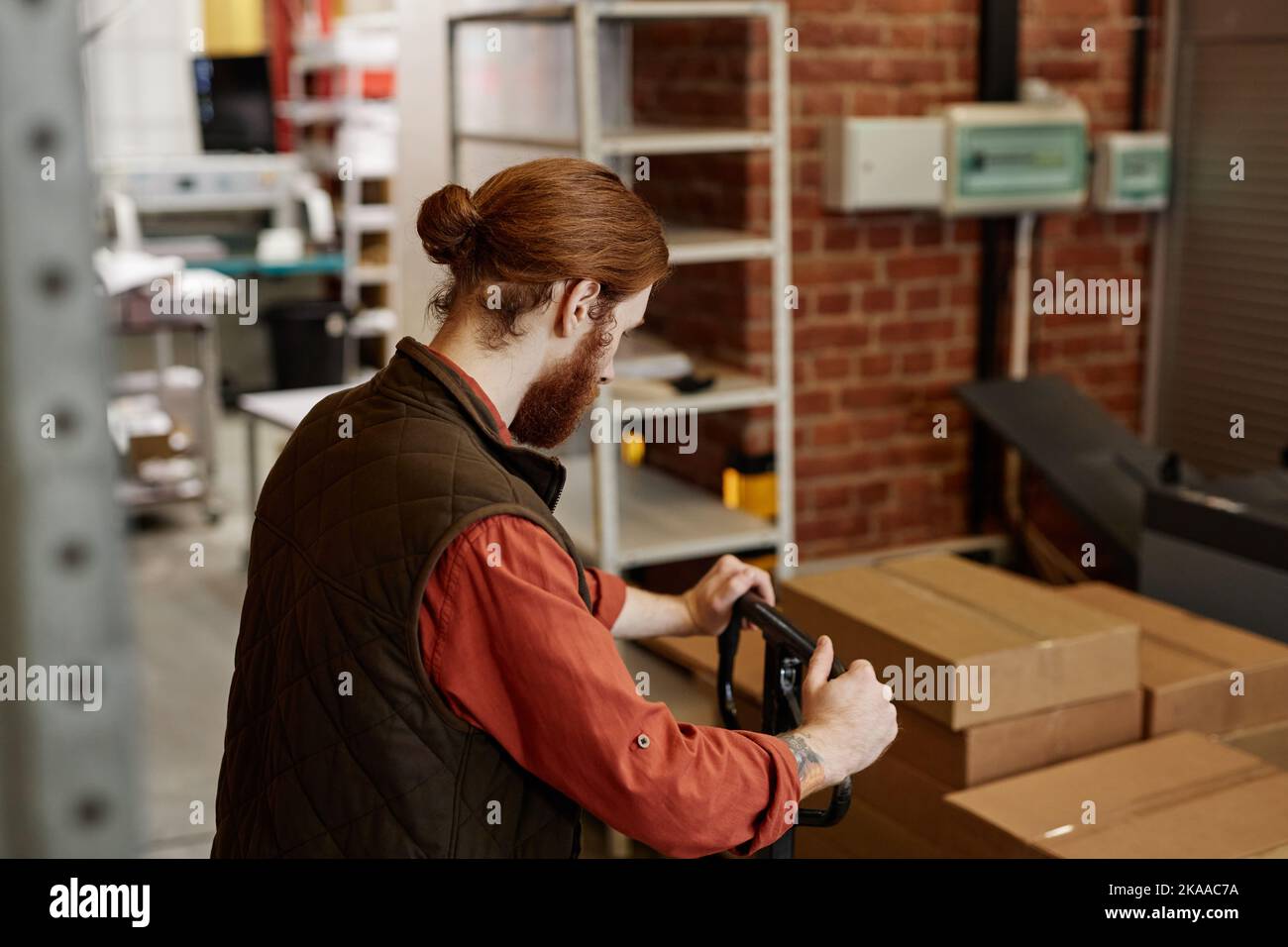 Side view portrait of male worker using pallet jack while moving boxes ...