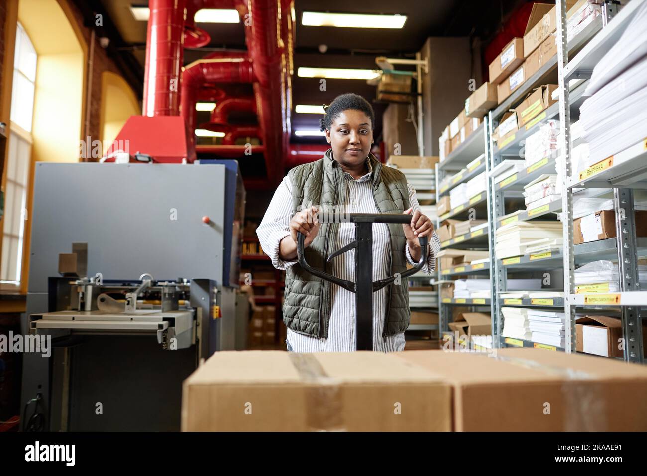 Front view portrait of female worker using pallet jack while moving ...