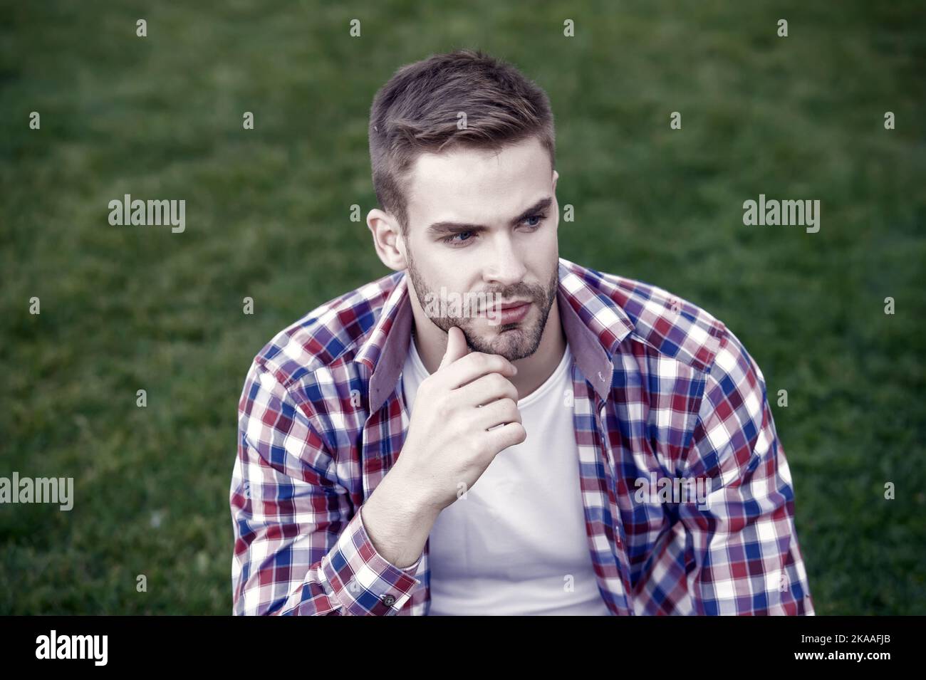 Never too young to start daily skincare. Young man sit on green grass ...