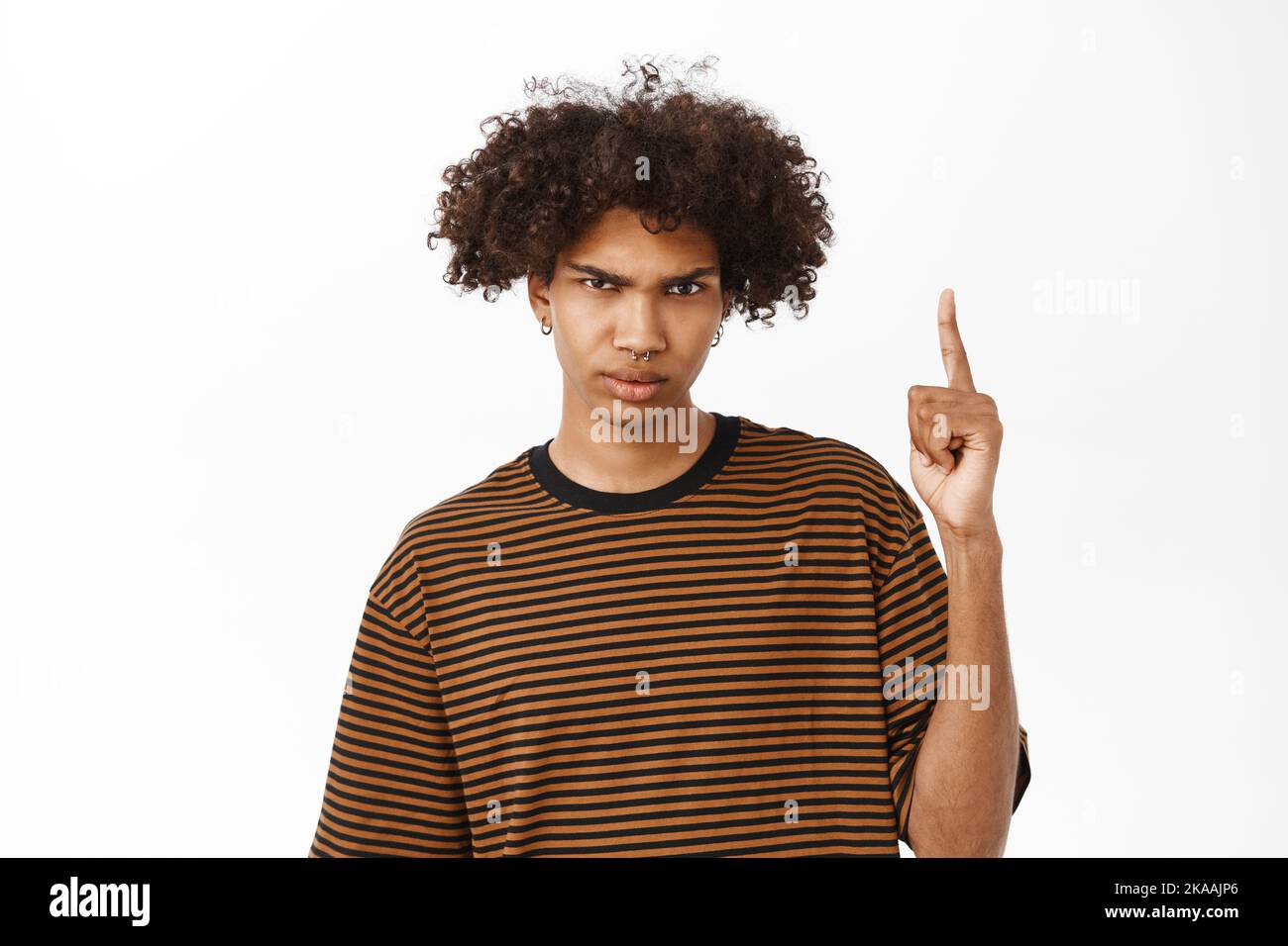 Angry young man pointing finger up, frowning and looking serious ...