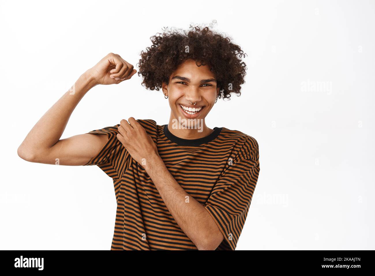 Handsome young slim boy, laughing and showing biceps, flexing muscles ...