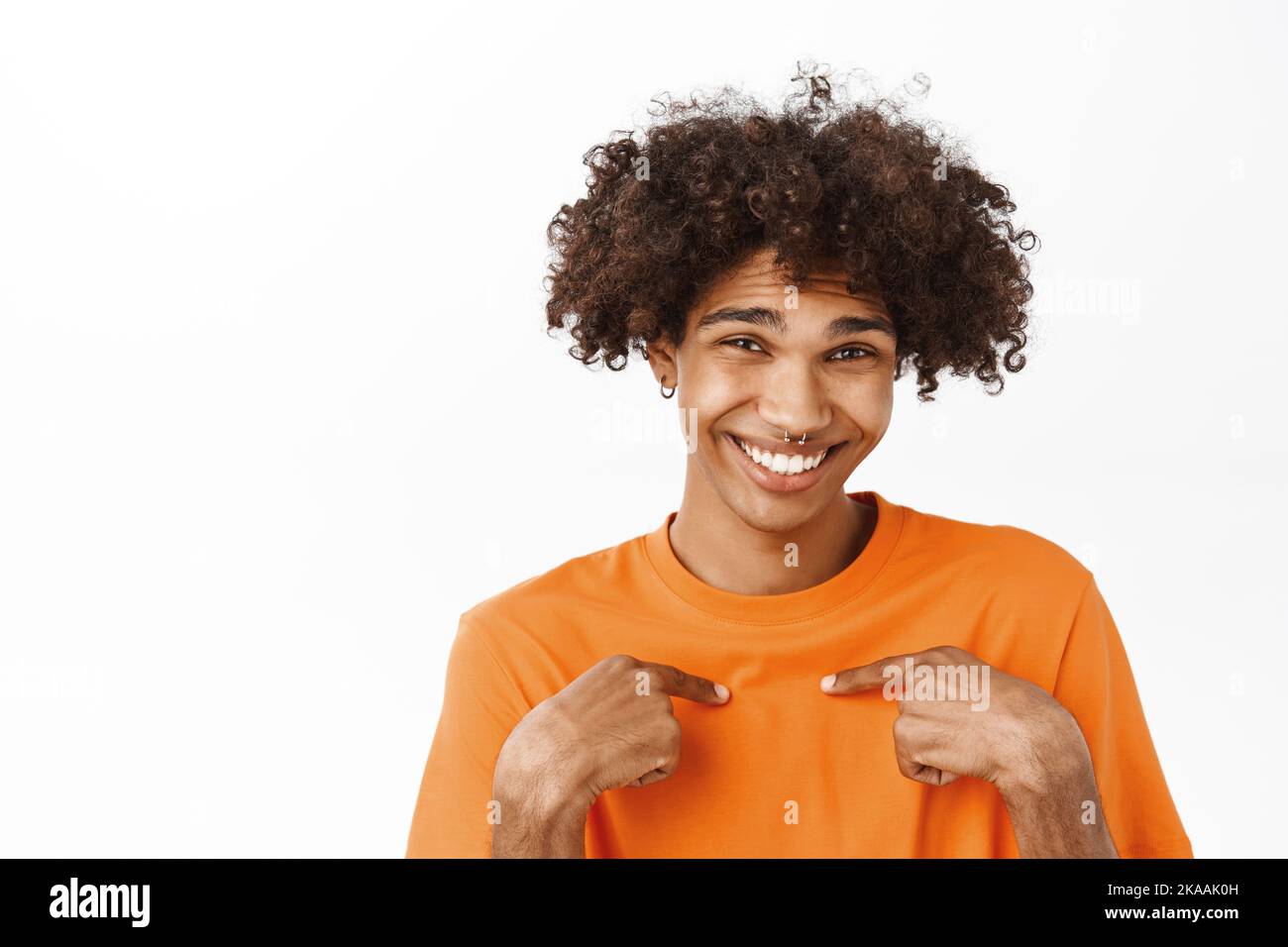 Close up of cute, gen-z guy with curly hair and piercing, pointing at ...