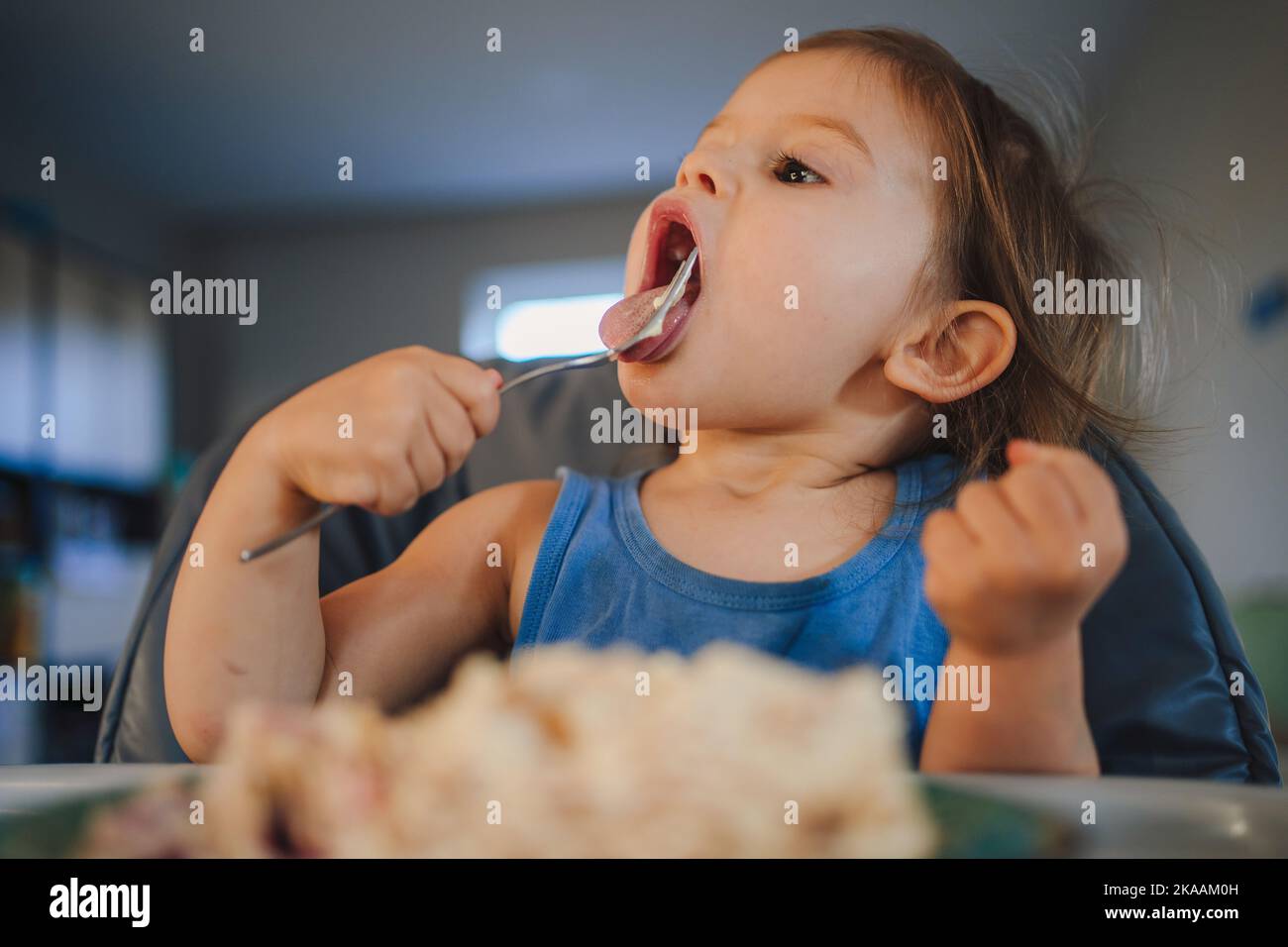 Portrait caucasian baby girl eating food from plate using fork, sitting ...