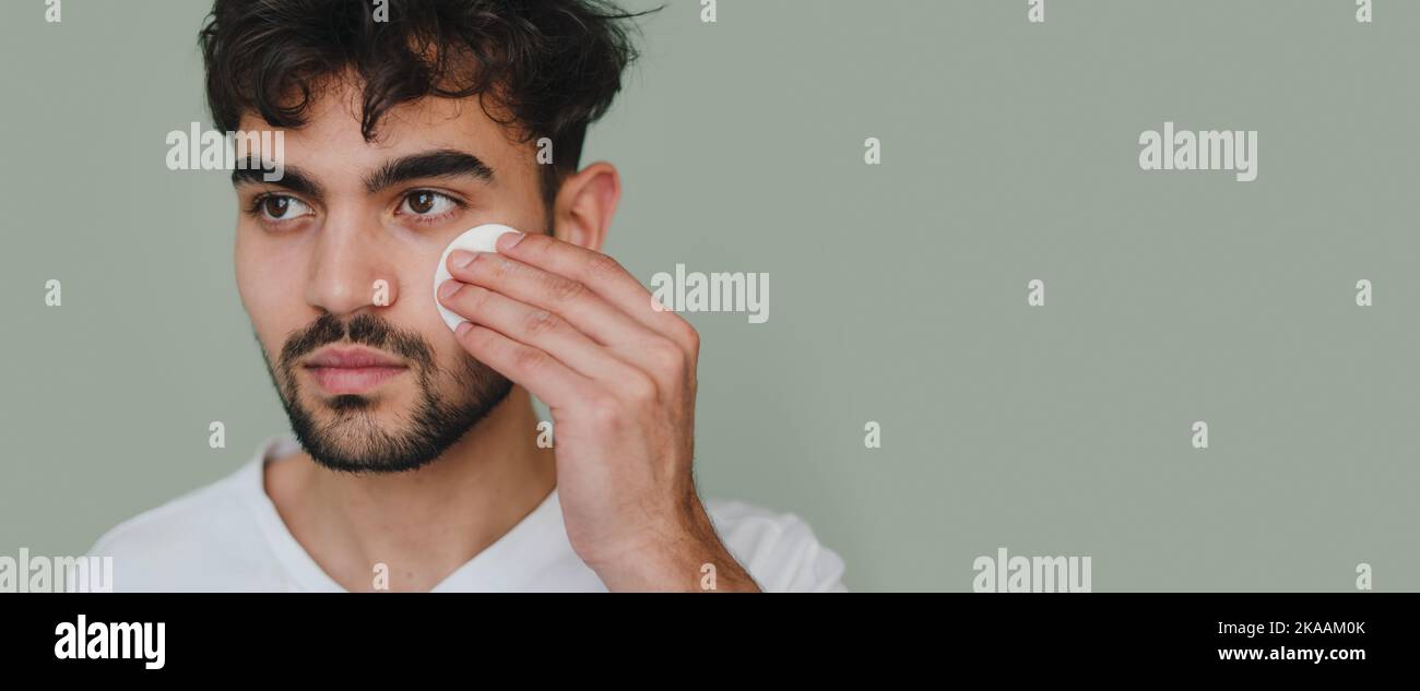 Attractive young man cleaning face skin with batting cotton pad over ...