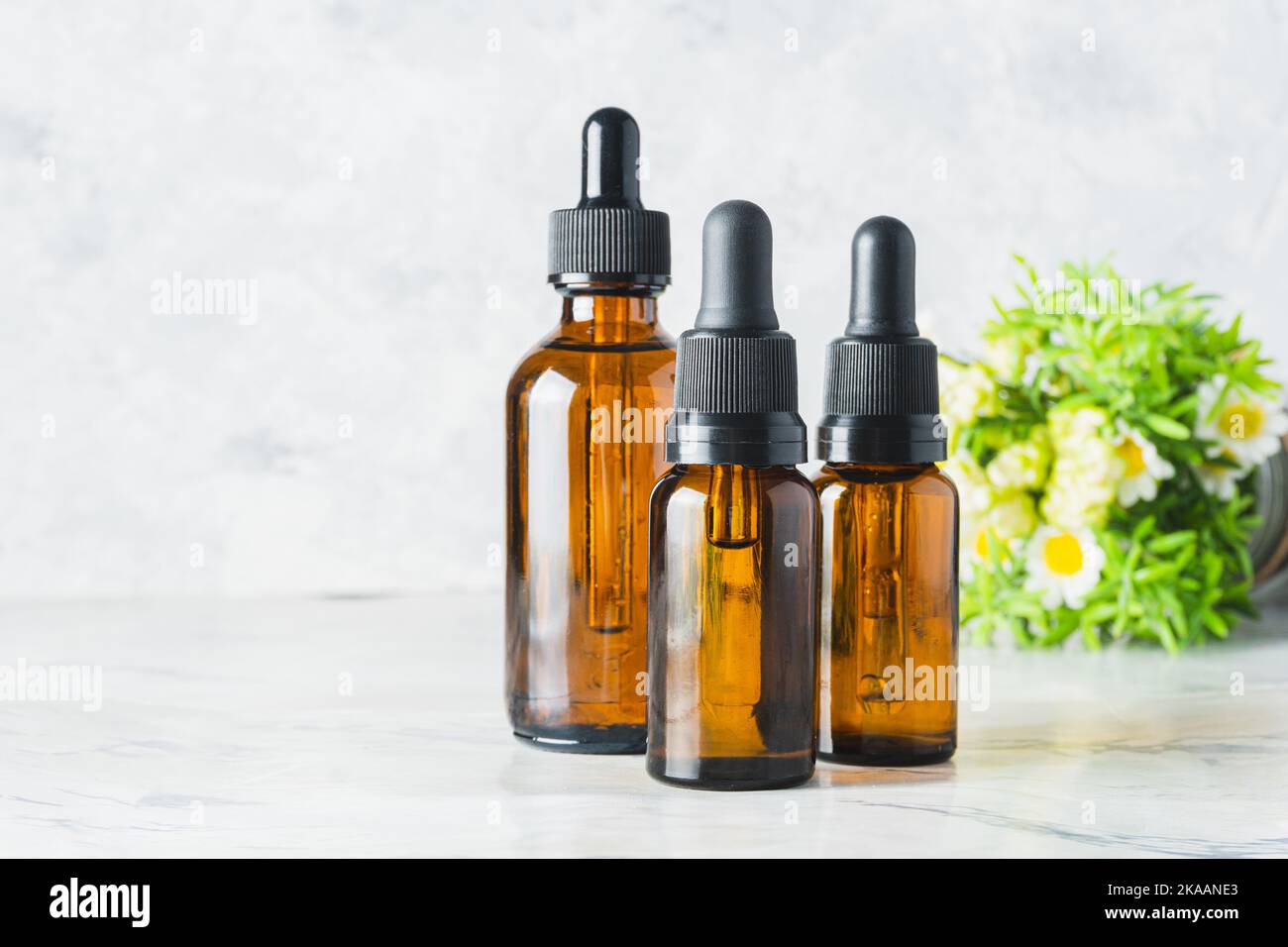 three essential oil dropper bottles with chamomile flowers out of focus ...