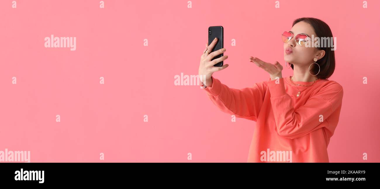 Beautiful young woman taking selfie on pink background with space for ...