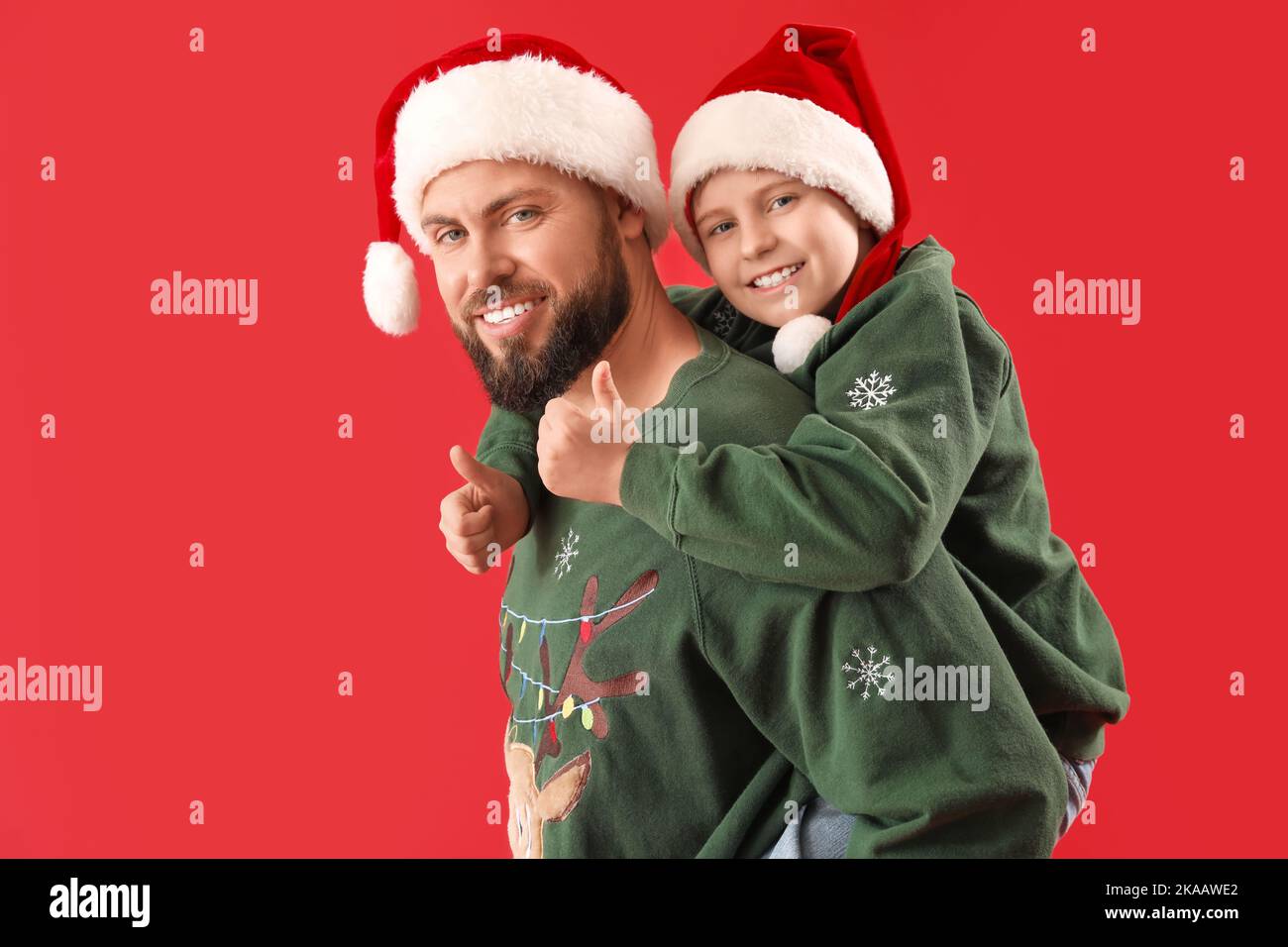 Happy father with his little son in Santa hats showing thumbs-up on red ...