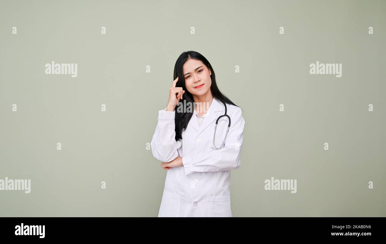 Thoughtful charming young Asian female doctor in uniform looking at the ...