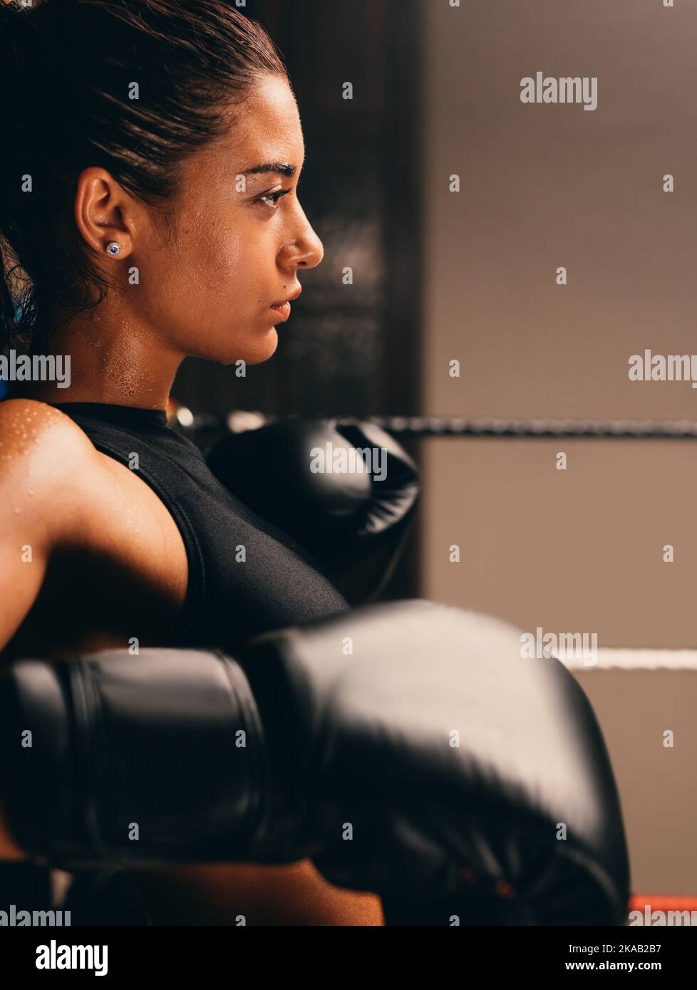 Sideview of a female boxer leaning against the ropes in a boxing ring ...
