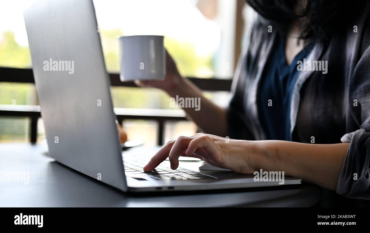 An Asian female freelancer remote working at the coffee shop, sipping ...