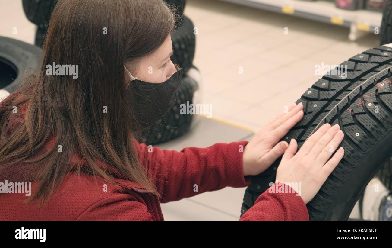 Girl in mask against virus buys studded tires for car in store. Close ...