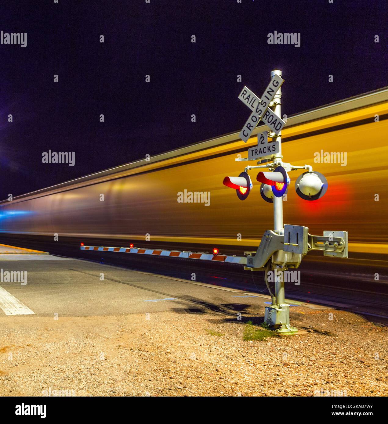 Railroad crossing with passing train by night Stock Photo - Alamy
