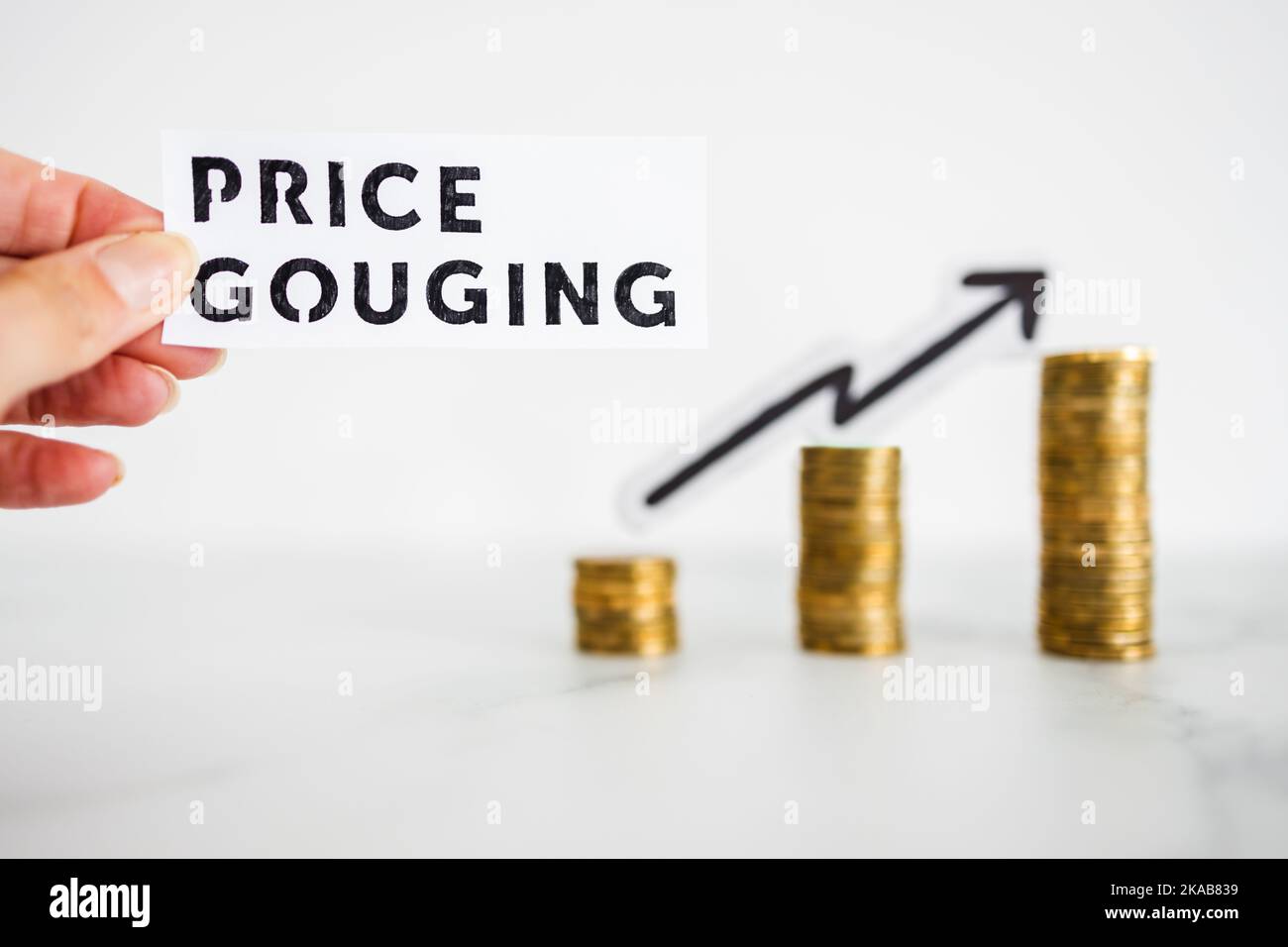 hand holding Price Gouging text in front of growing stacks of coins in ...