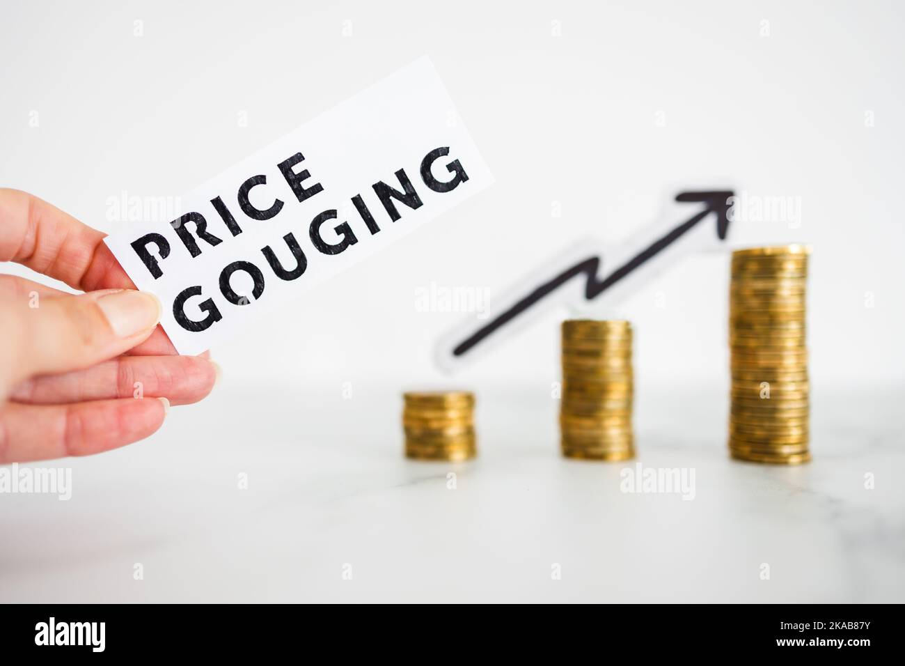 hand holding Price Gouging text in front of growing stacks of coins in ...