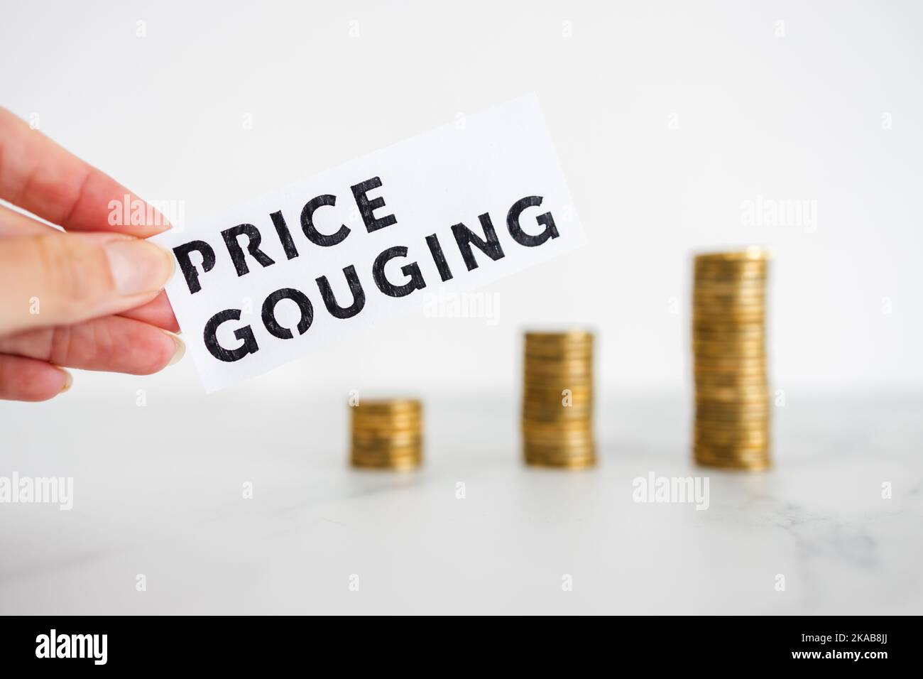 hand holding Price Gouging text in front of growing stacks of coins in ...