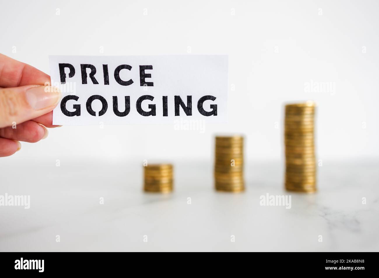 hand holding Price Gouging text in front of growing stacks of coins in ...