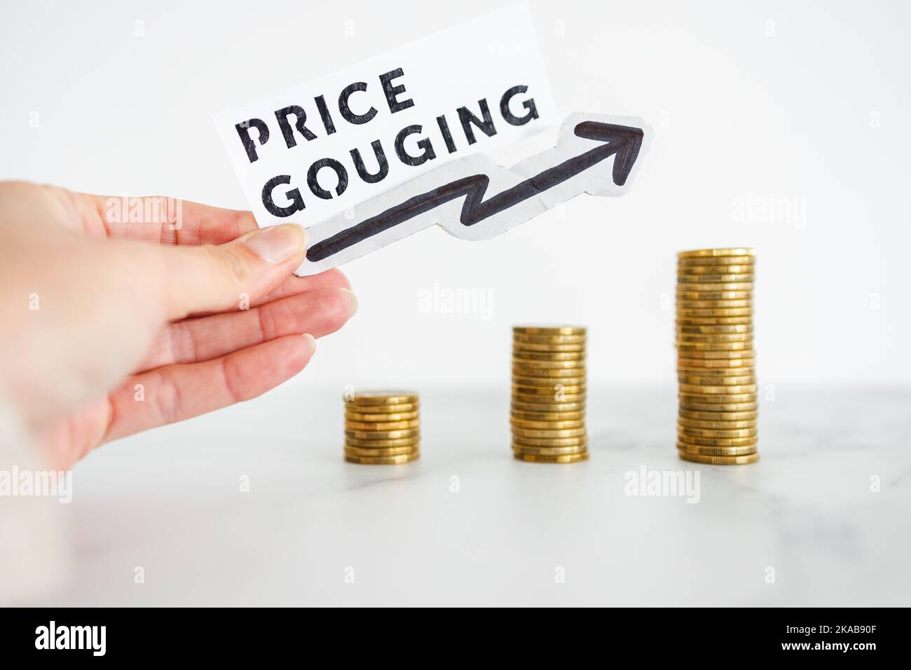 hand holding Price Gouging text in front of growing stacks of coins in ...