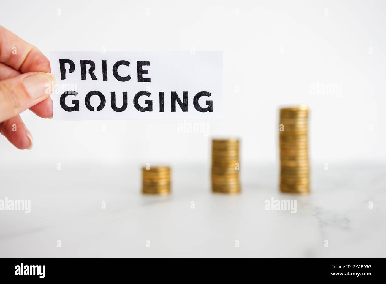 hand holding Price Gouging text in front of growing stacks of coins in ...