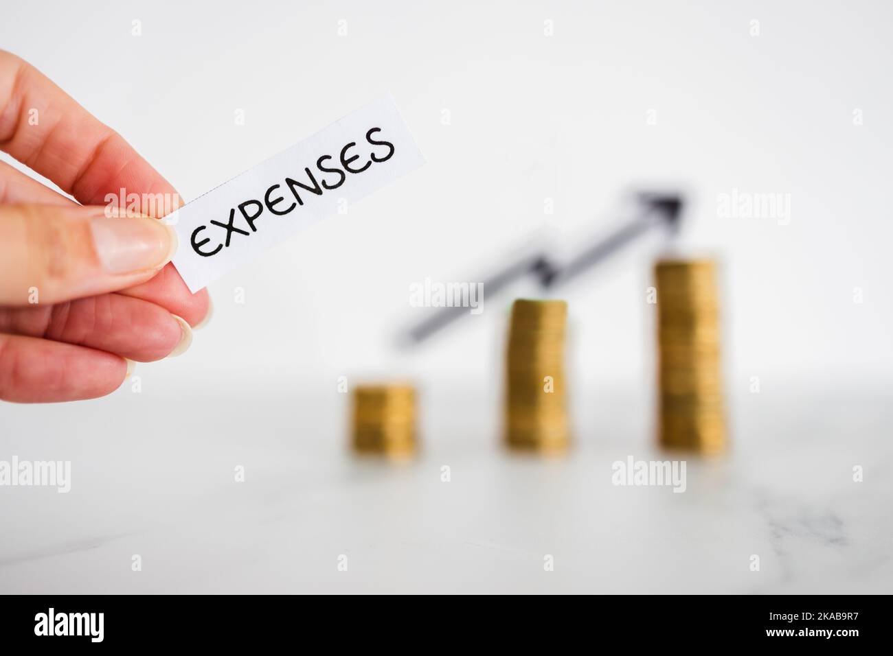 hand holding Expenses text in front of growing stacks of coins with ...