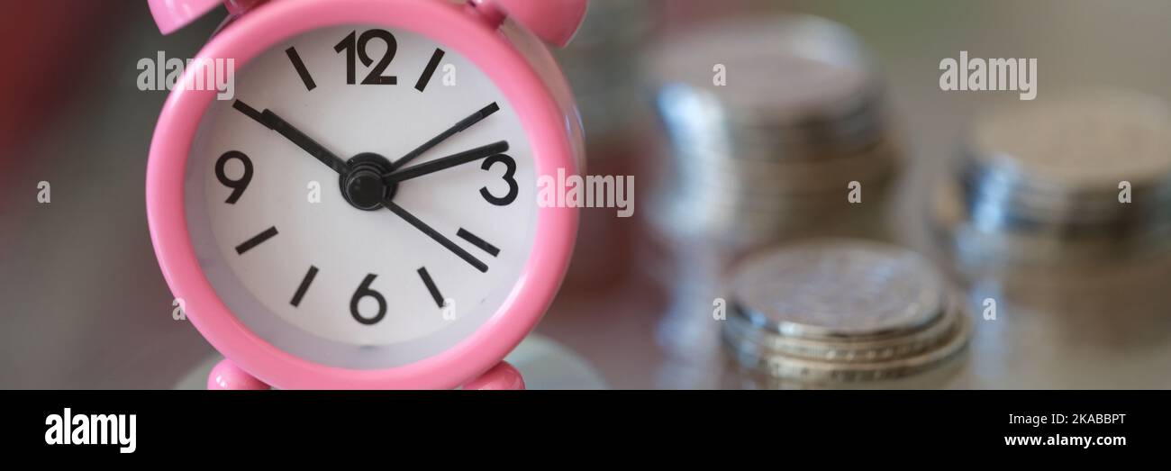Pink alarm clock compass and stacks of coins closeup Stock Photo - Alamy