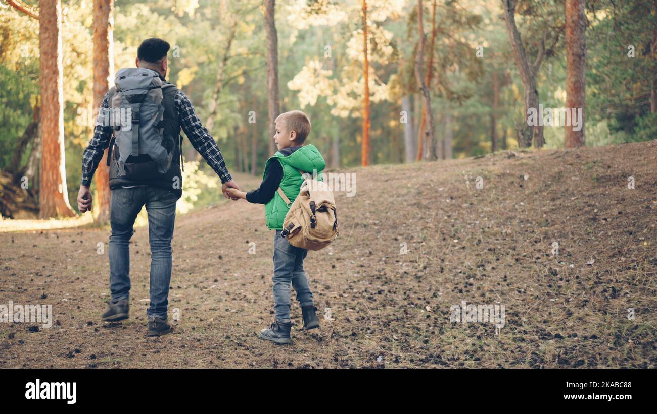 Back view of happy family child and caring father walking in forest ...
