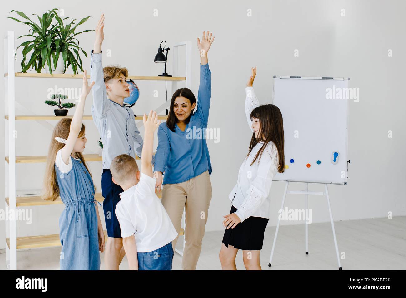 Happy children and educator raising hands up standing in modern ...
