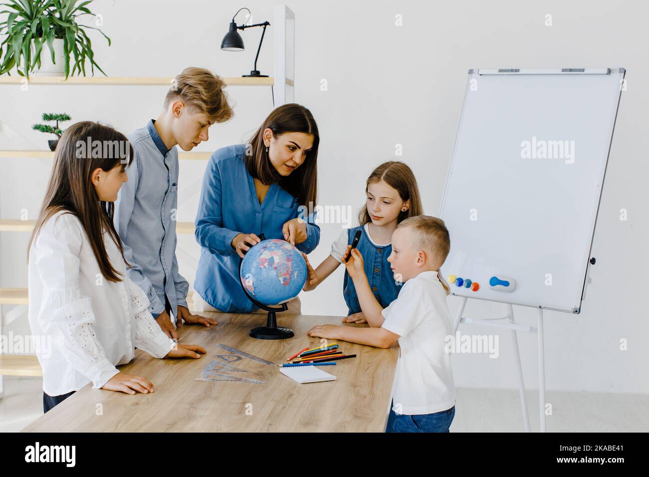 Teacher and children in class are looking at globe, teacher helps explain the lesson to the ...